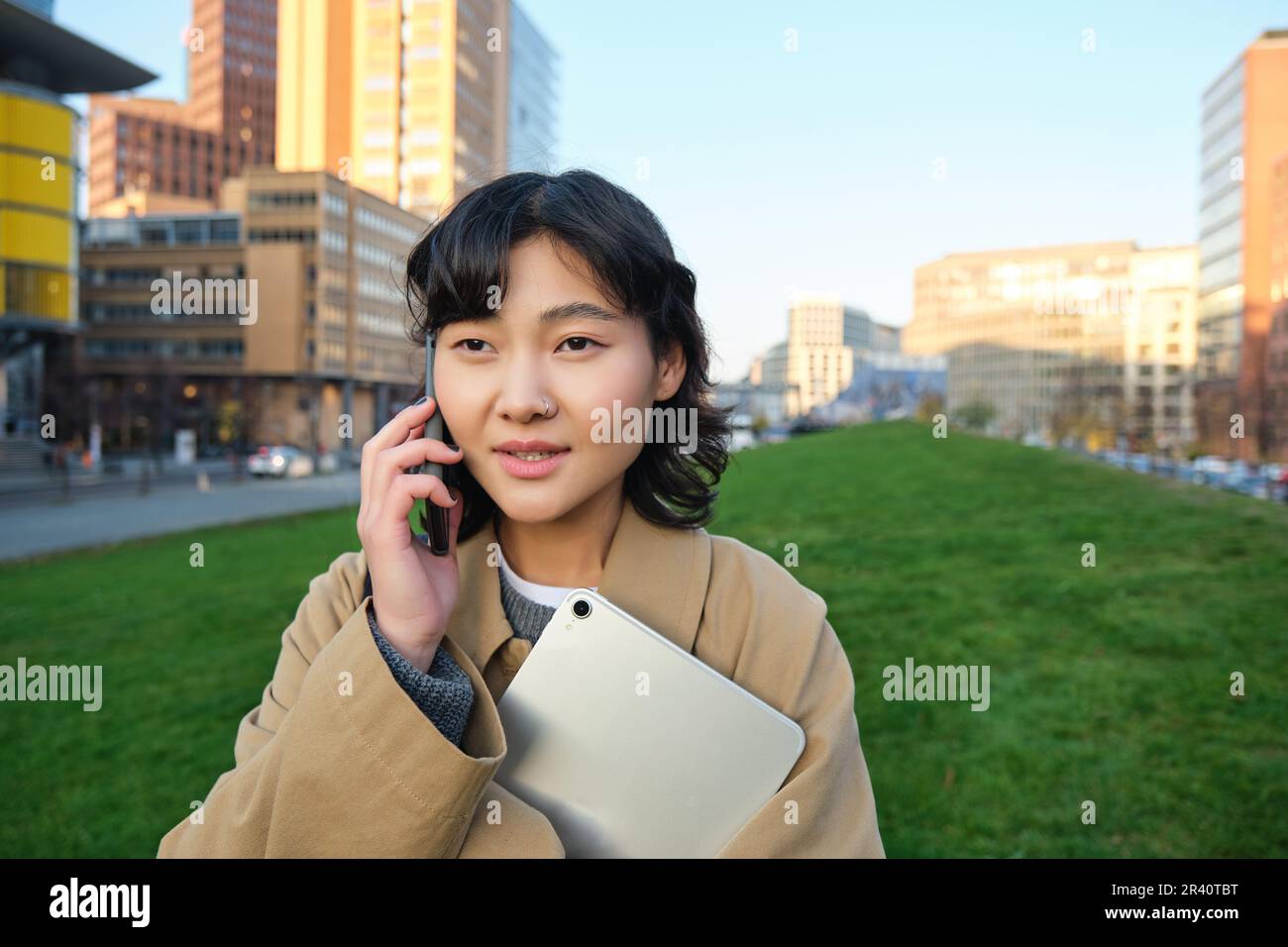 Stylish smiling girl, university student in trench coat, holds tablet ...