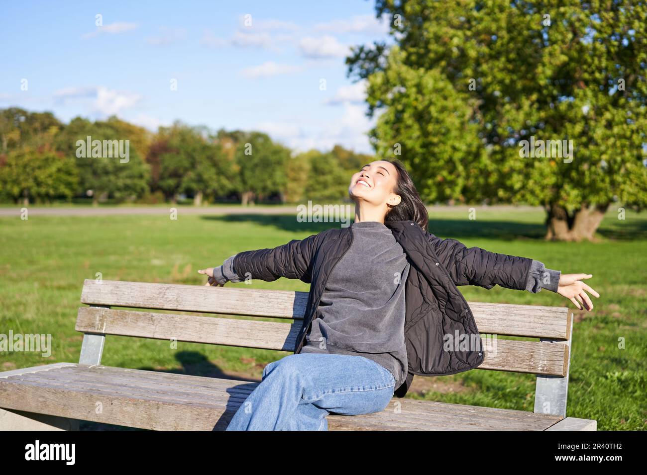 Portrait of young woman in outdoor clothes, sitting on bench relaxed ...