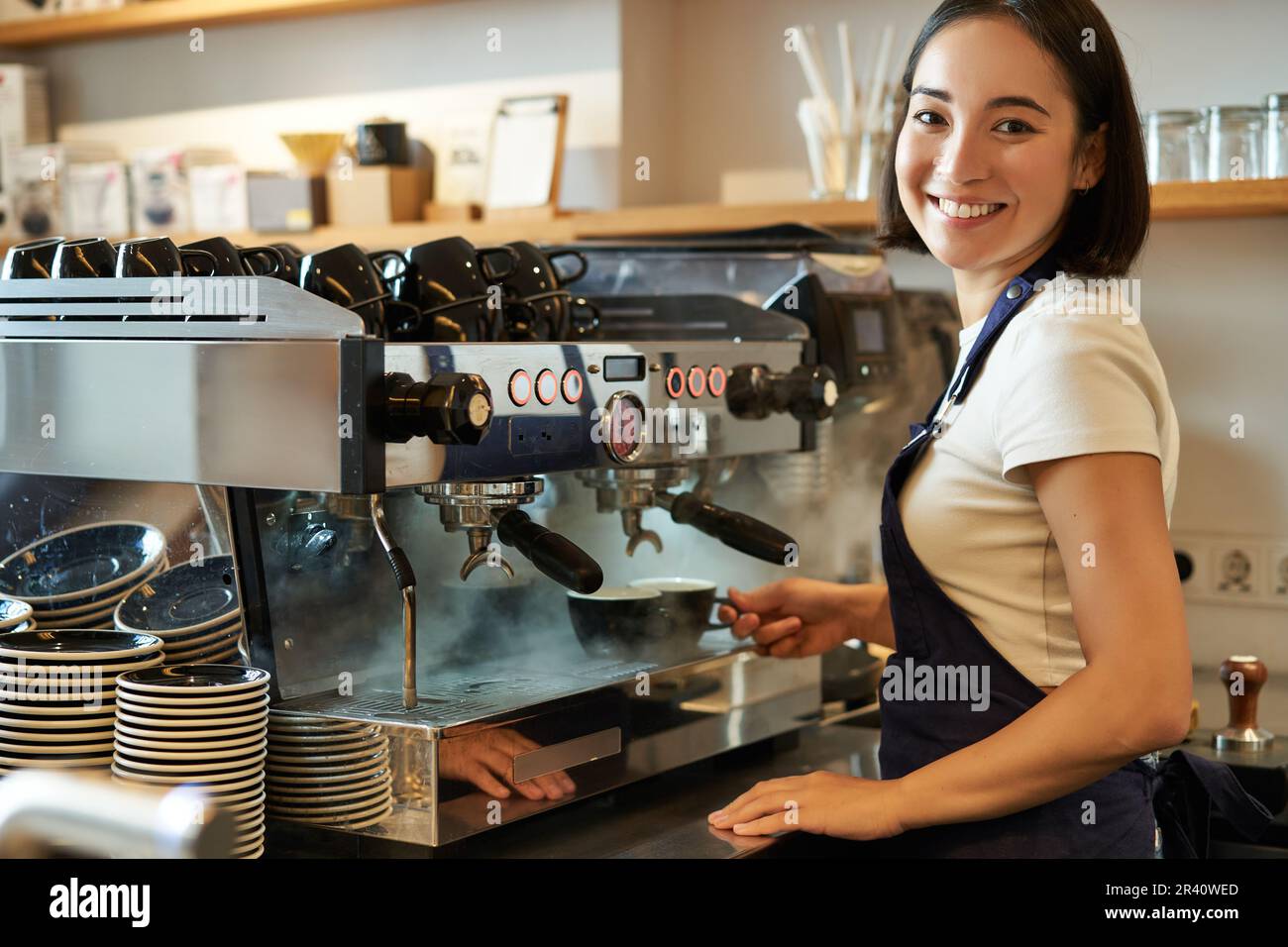 Smiling cute korean girl, barista working with coffee machine, prepare ...