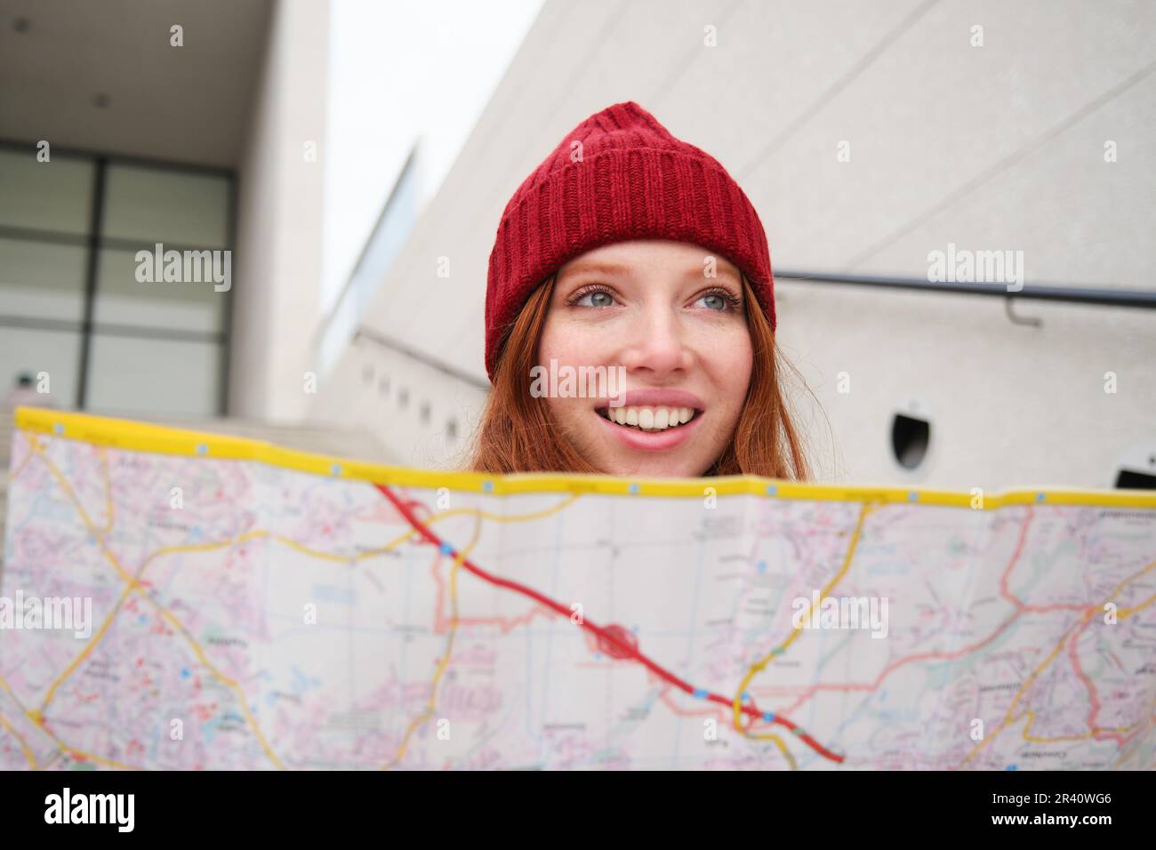 Beautiful girl tourist sits on stairs with city map, plans her journey, looks for direction ...