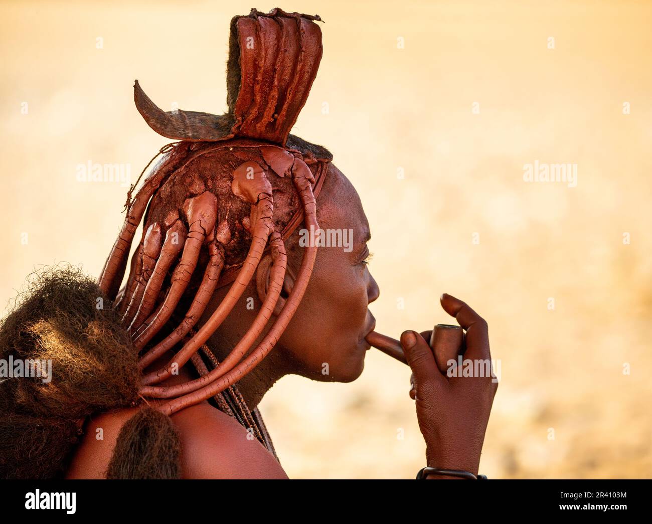 Portrait of a young woman of the Himba tribe with a smoking pipe and a ...