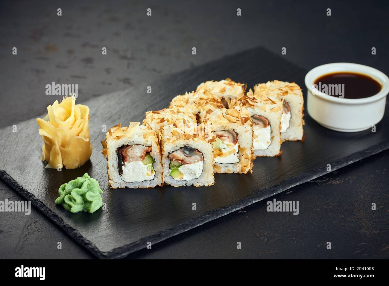 Sushi roll with eel, avocado, cream cheese and tuna shavings on dark ...
