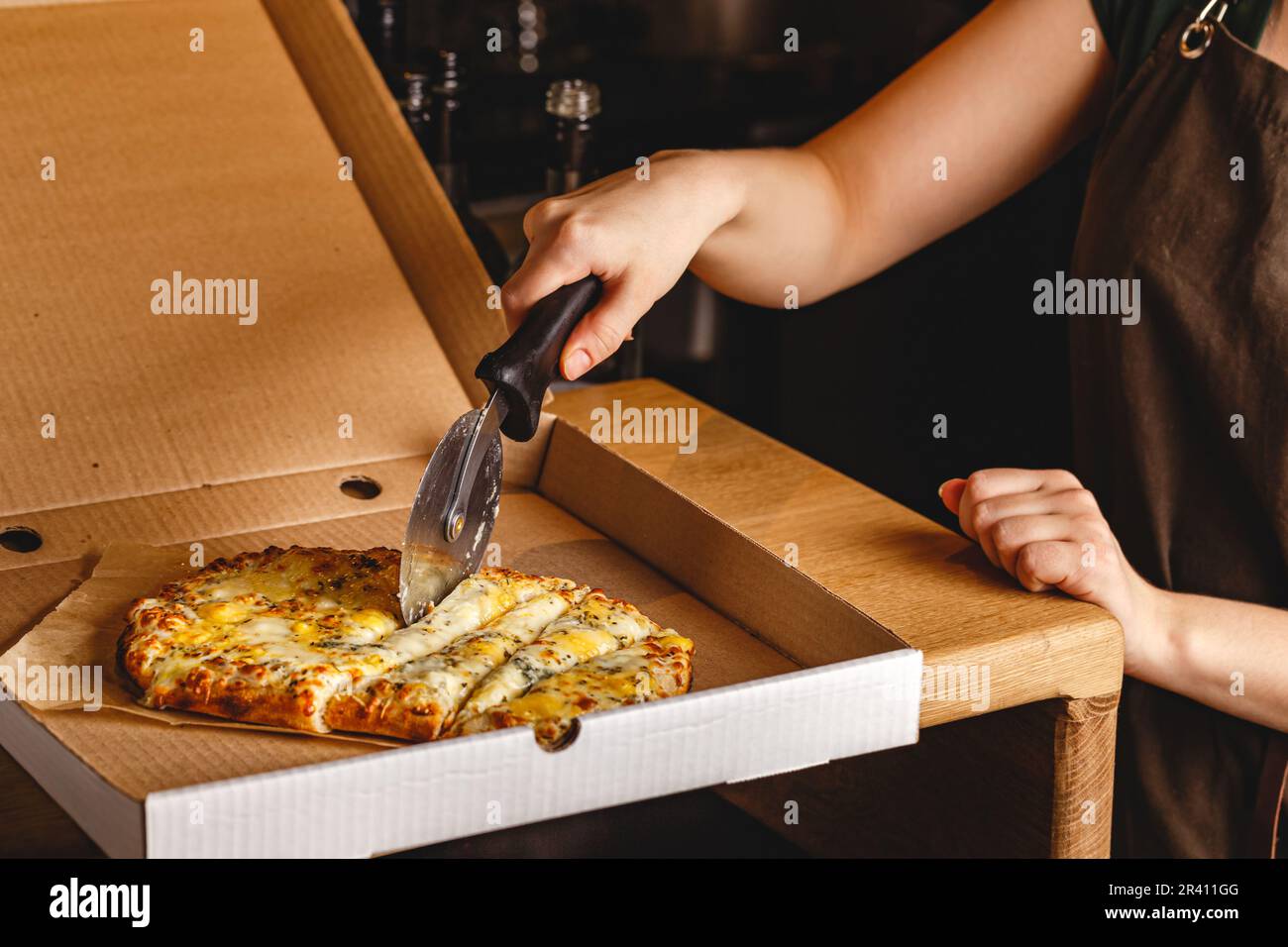Woman's hand cuts pizza in box with roller knife. Roman square pizza or ...