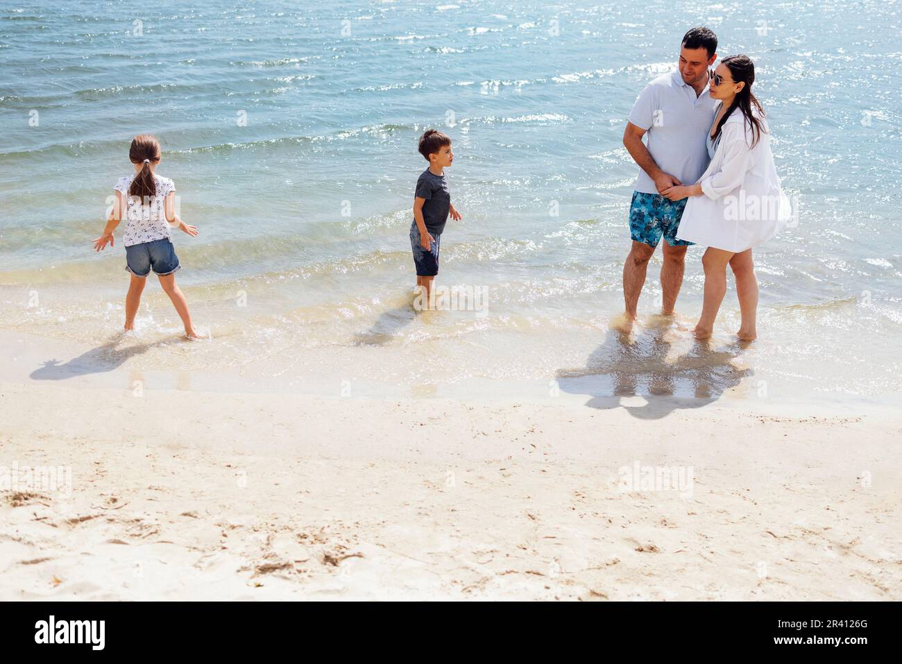 Son and daughter run on the water and splash on their smiling parents ...