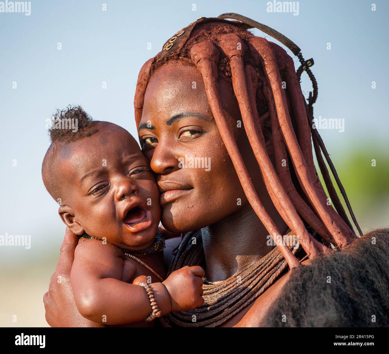 Portrait of a young woman of the Himba tribe with a small child in her ...