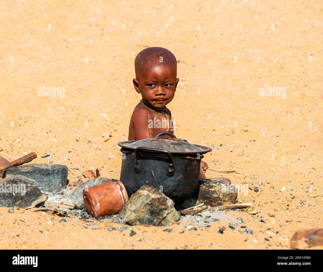 Small child of the Himba tribe is sitting near a large pot of food ...