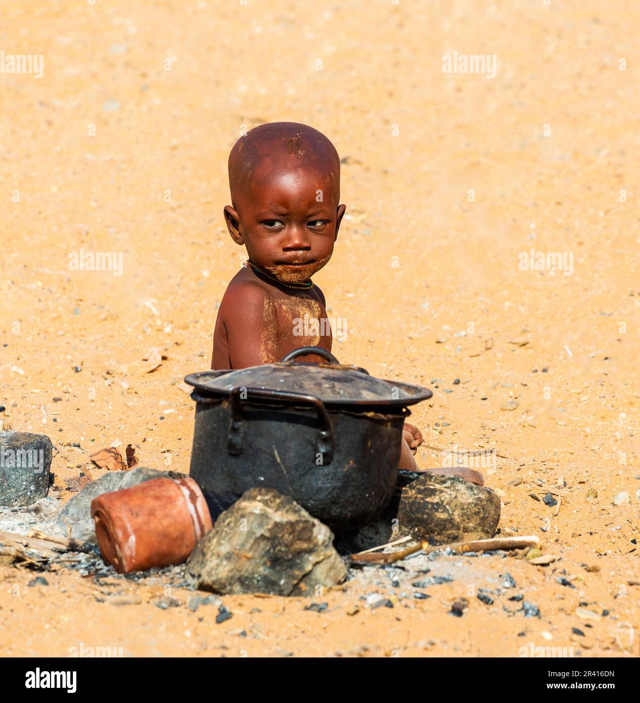 Small child of the Himba tribe is sitting near a large pot of food ...