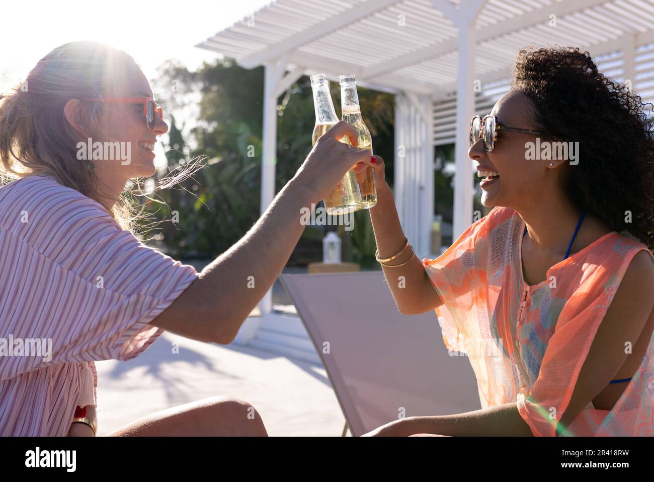 Happy diverse female friends having party by swimming pool, sitting on ...