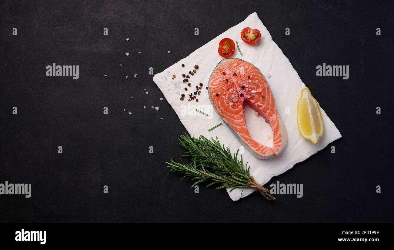 Raw salmon steak on a white board, lemon slices, spices. Top view on ...