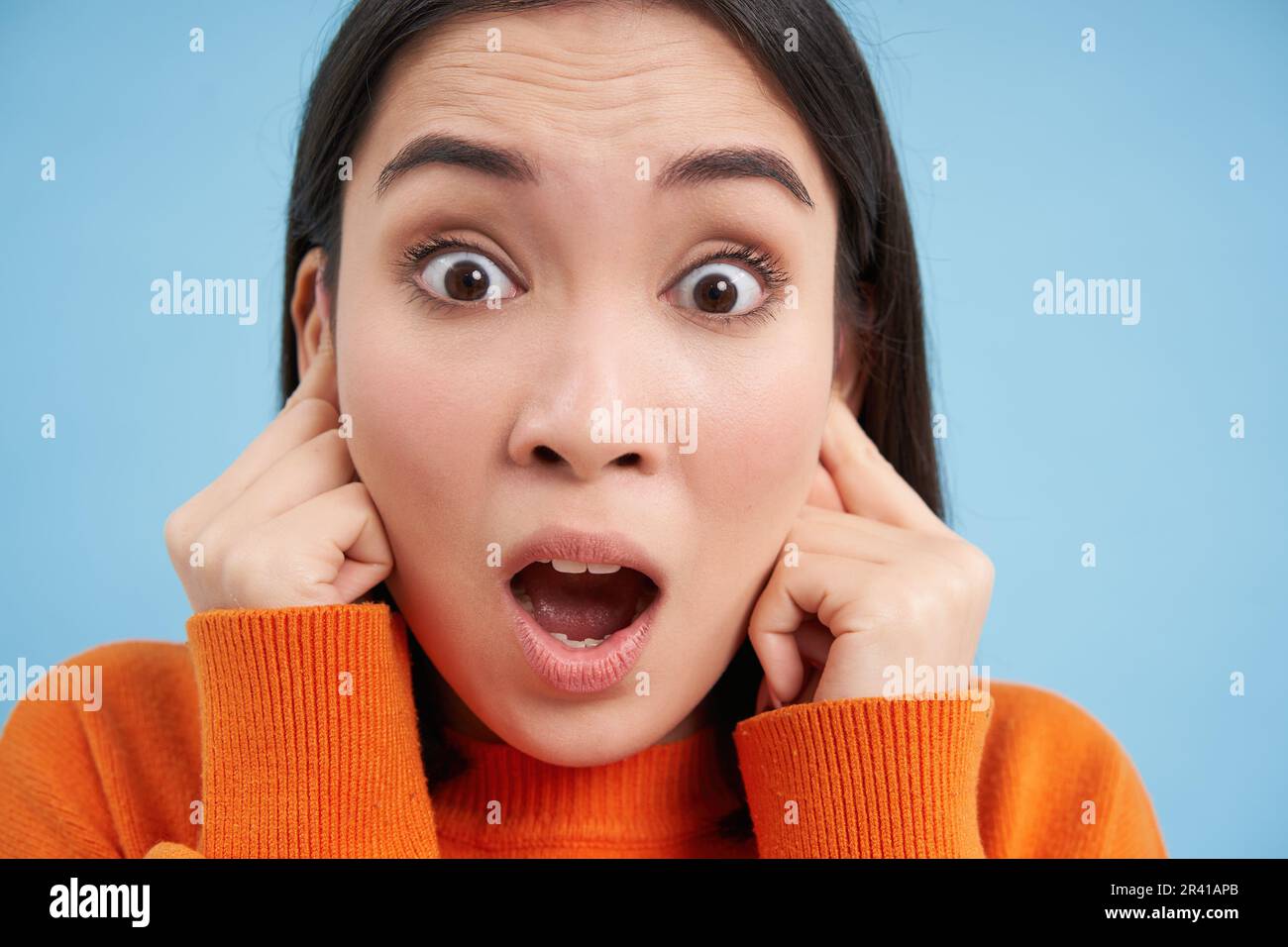 Close up portrait of asian girl shuts her ears from loud noise, looks ...