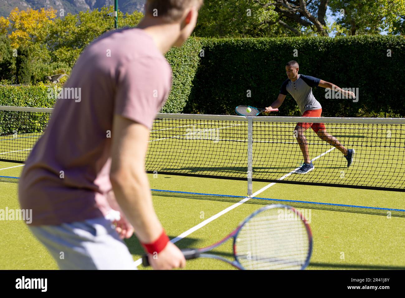 Happy diverse male friends playing tennis together at tennis court ...