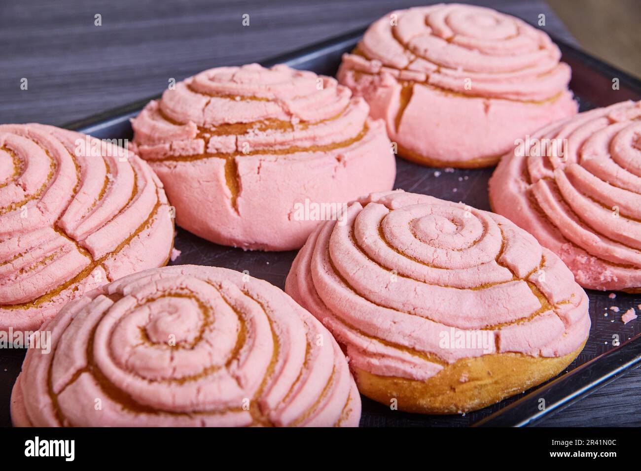 Tray of strawberry conchas Mexican sweet bread pastry baked good seashell swirl frosting pattern ...