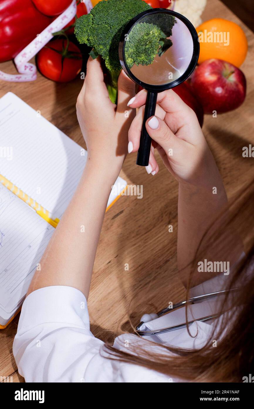 A female nutritionist looks through a magnifying glass at broccoli in ...