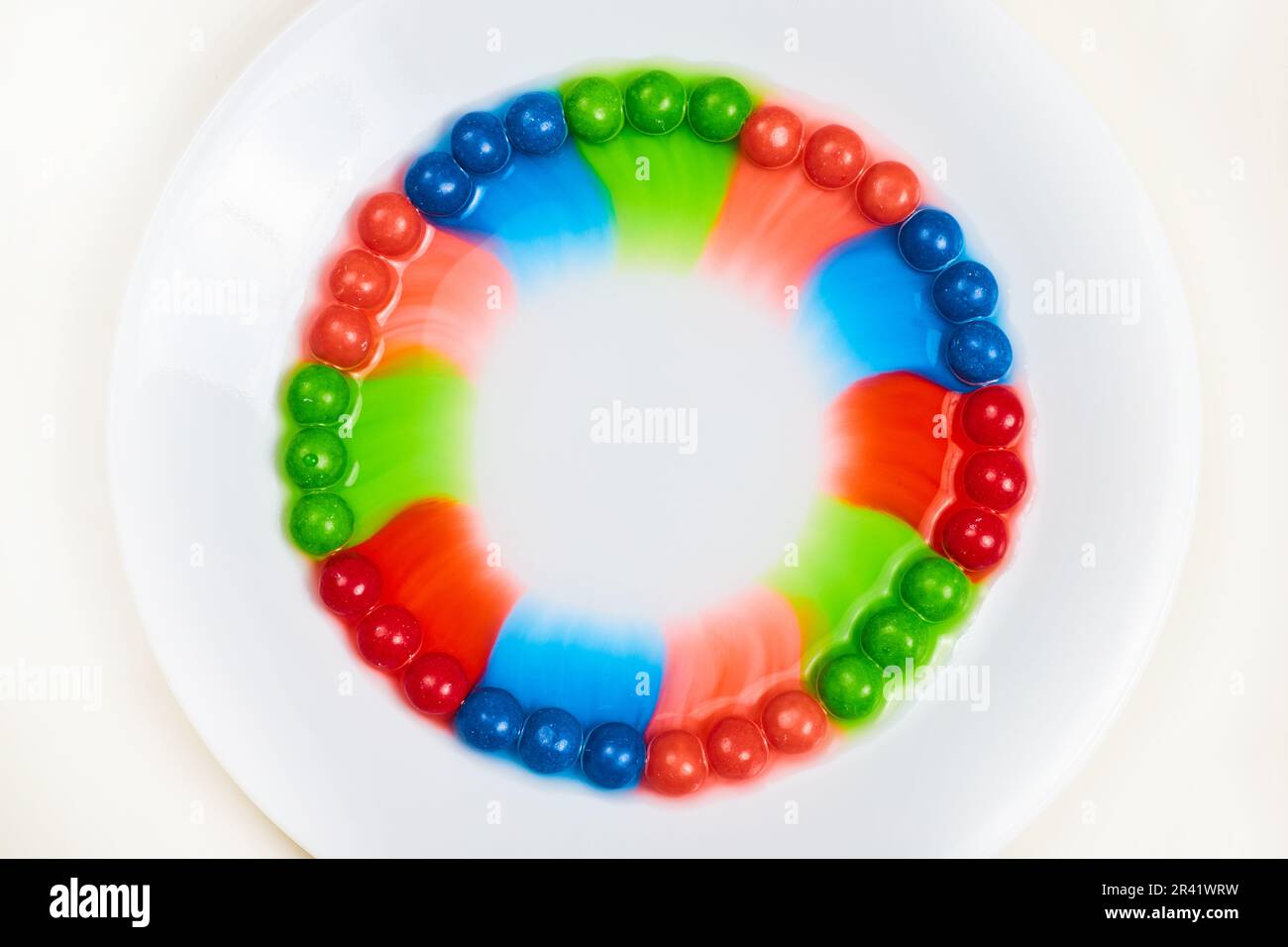 Circle of red and blue and green bleed colors into water as skittles ...