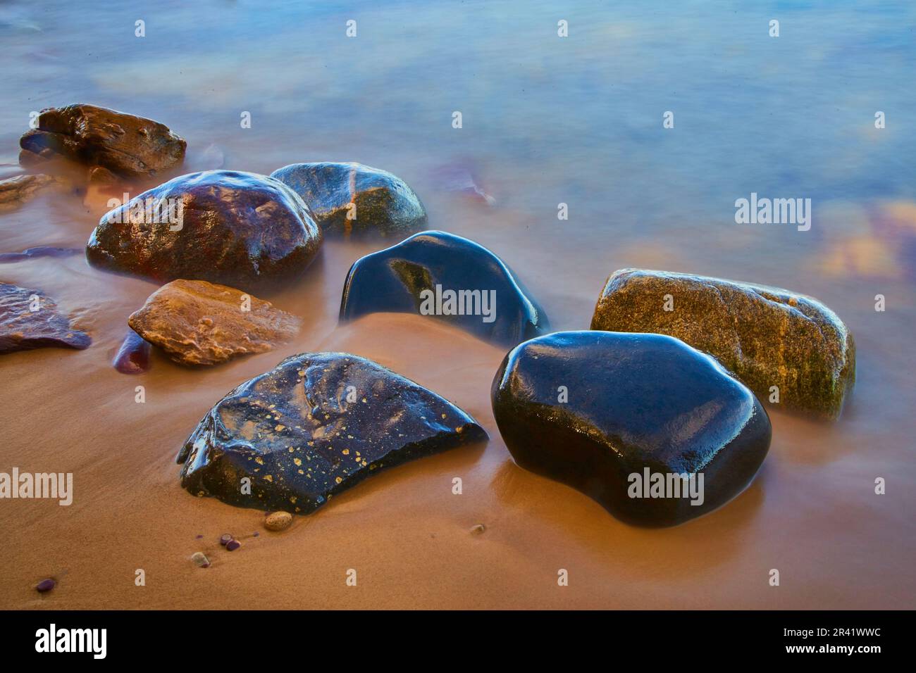 Sandy beach shore with smooth wet rocks of precious stones washed ...
