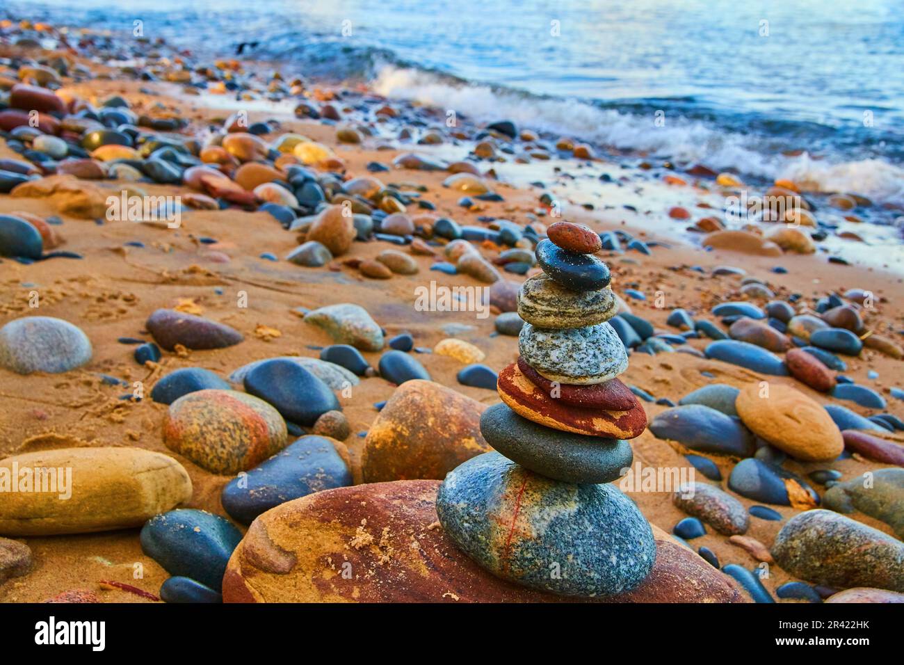 Cairn of stacked smooth lakebed stones with sandy shore and crashing ...