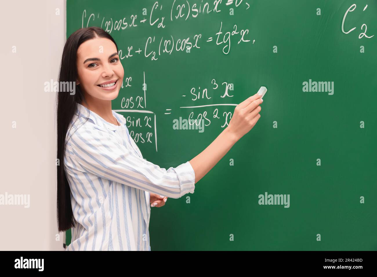 Happy teacher explaining mathematics at chalkboard in classroom Stock ...