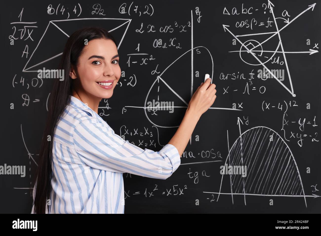 Happy teacher explaining mathematics at chalkboard in classroom Stock ...