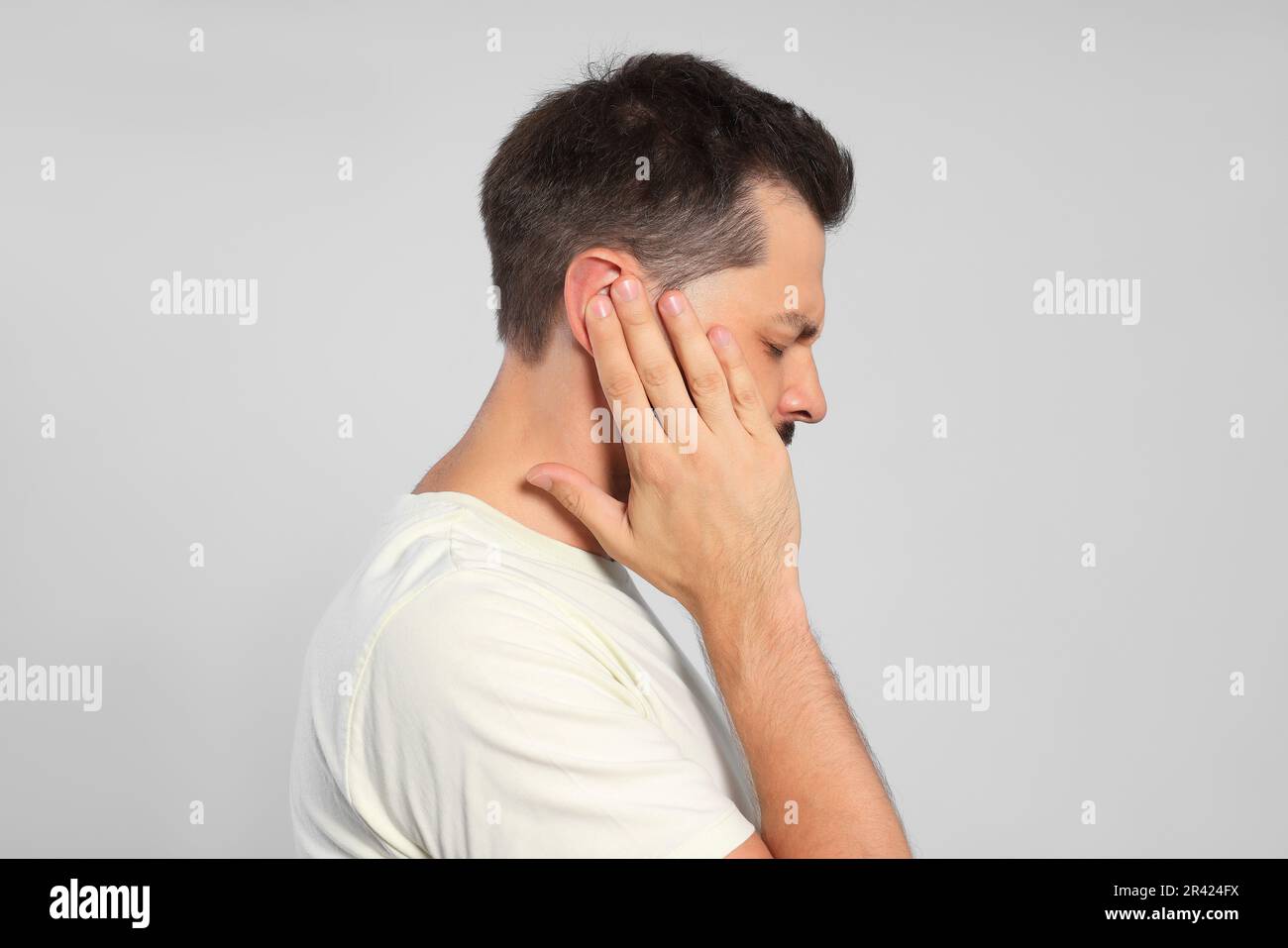 Man suffering from ear pain on grey background Stock Photo - Alamy