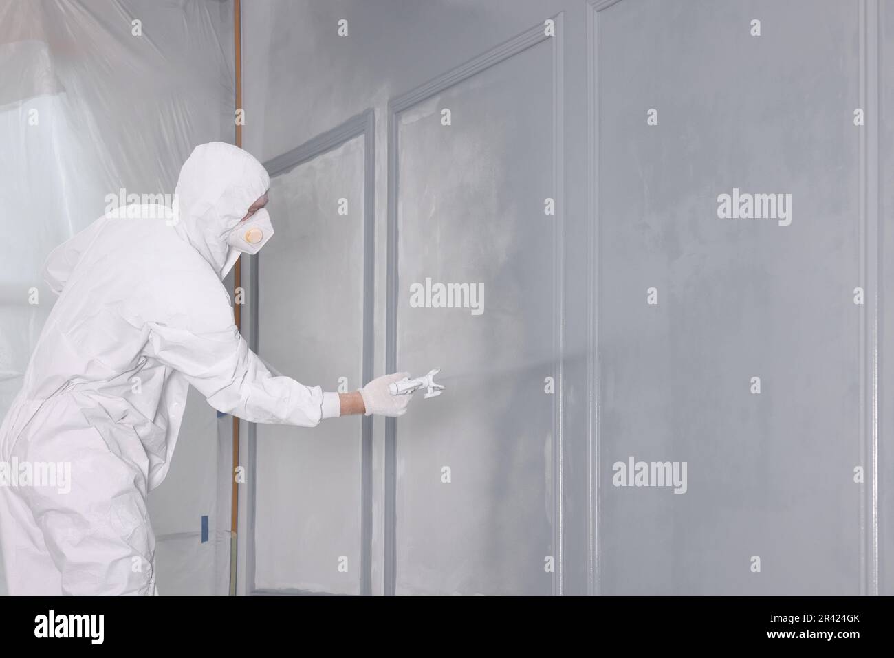 Decorator dyeing wall in grey color with spray paint, space for text ...