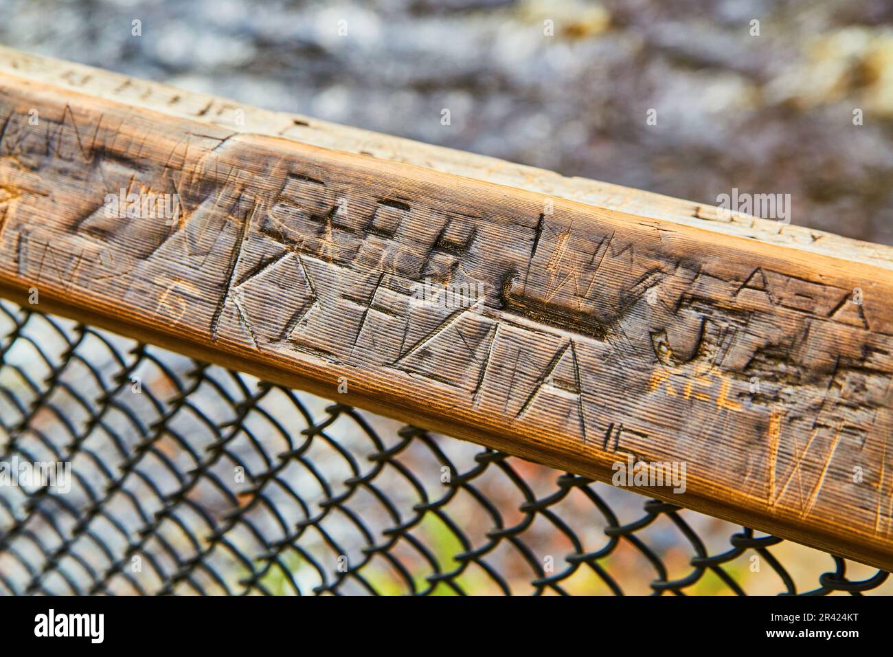 Names and symbols etched into old wood railing with blurred cliff wall ...