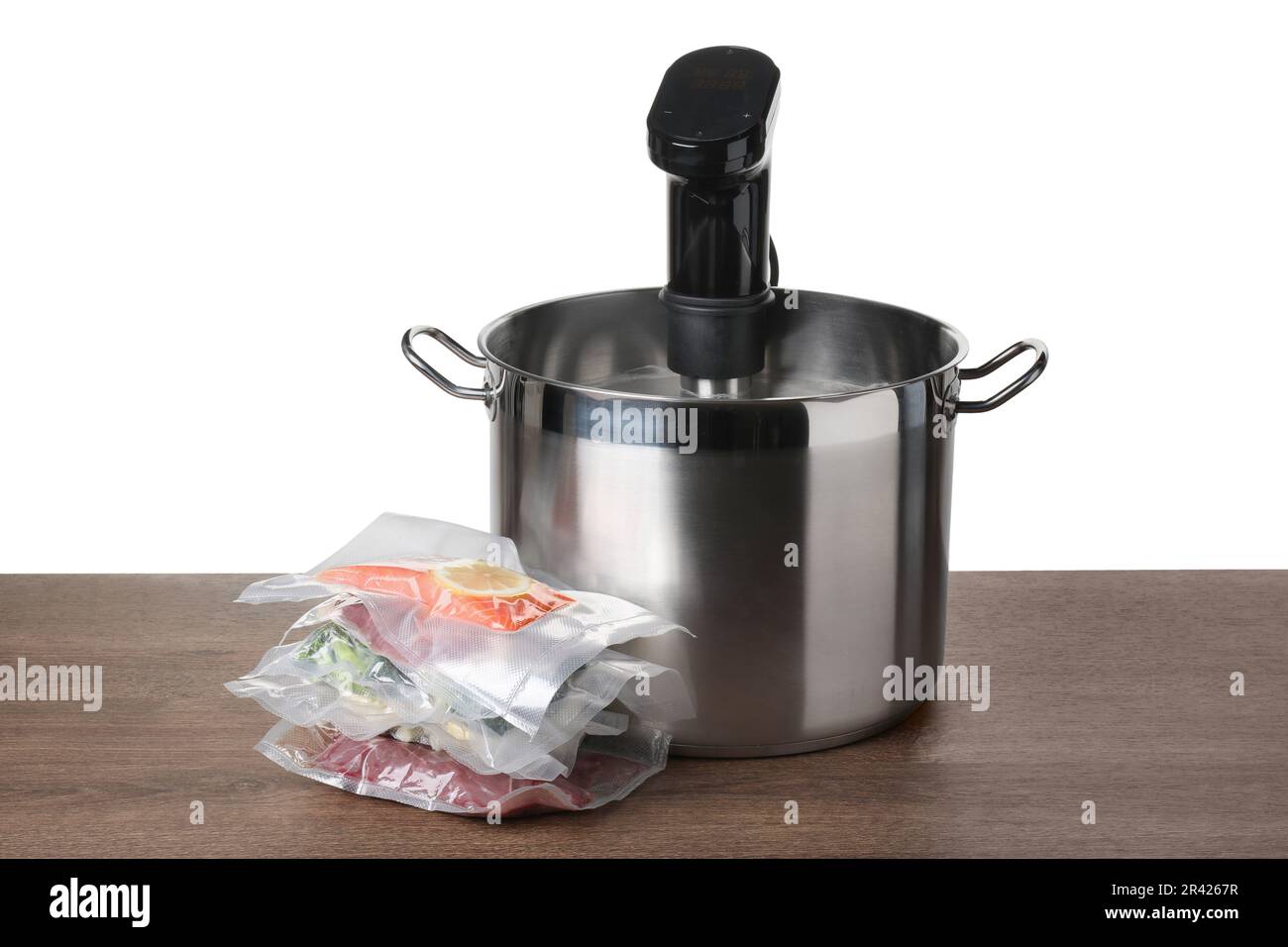 Sous vide cooker in pot and vacuum packed food products on wooden table ...