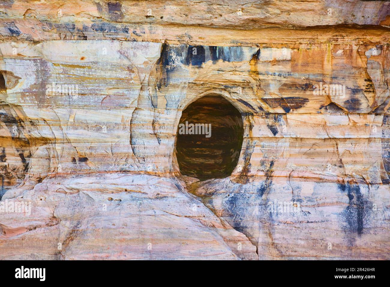 Cave opening in Pictured Rocks cliff wall of gold, rust, and mineral ...