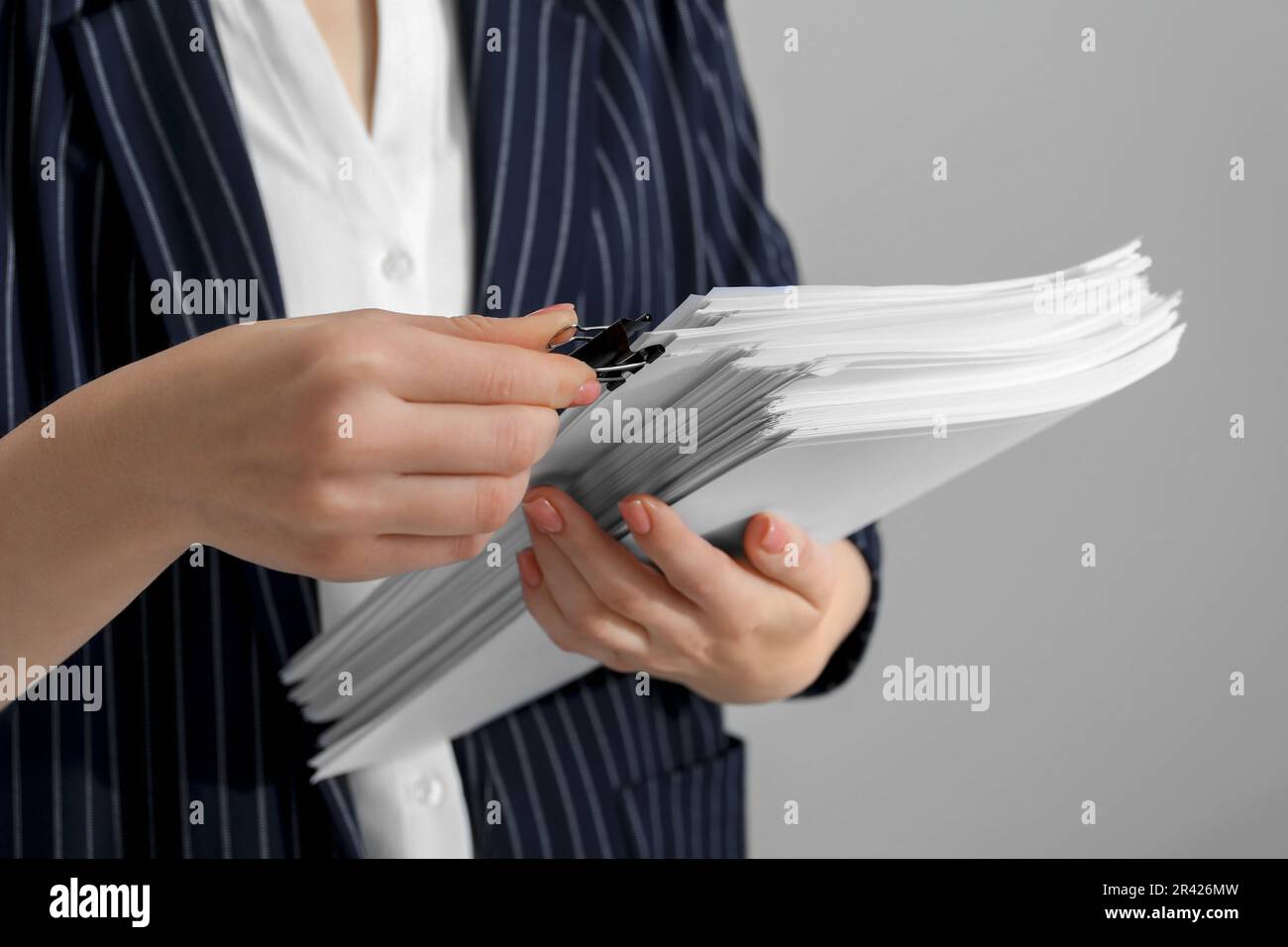 Woman attaching documents with metal binder clip on grey background ...