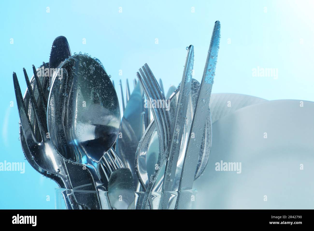 Washing silver cutlery and plates in water on light blue background ...