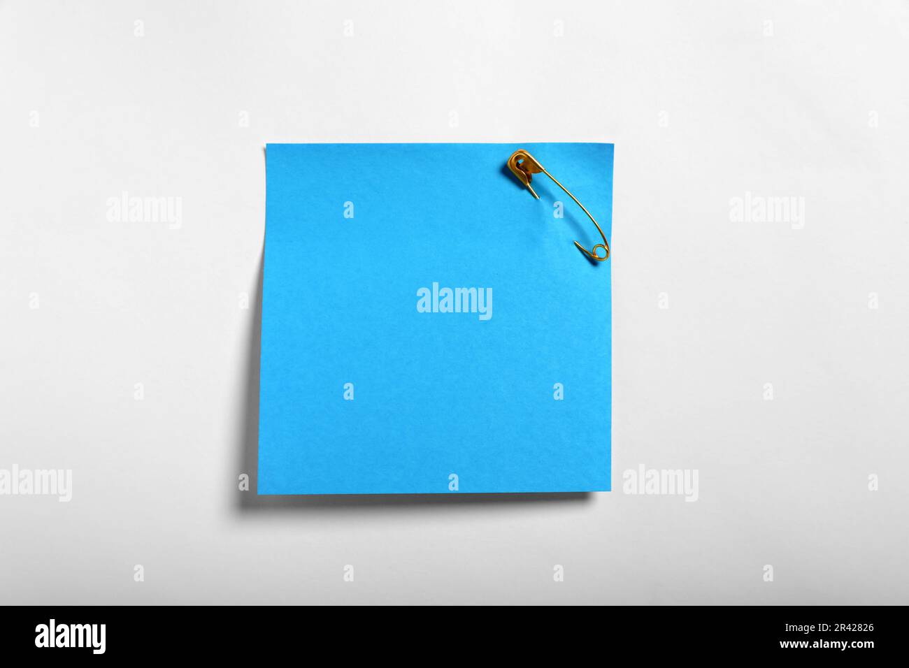 Blue paper note attached with safety pin to white background, top view ...