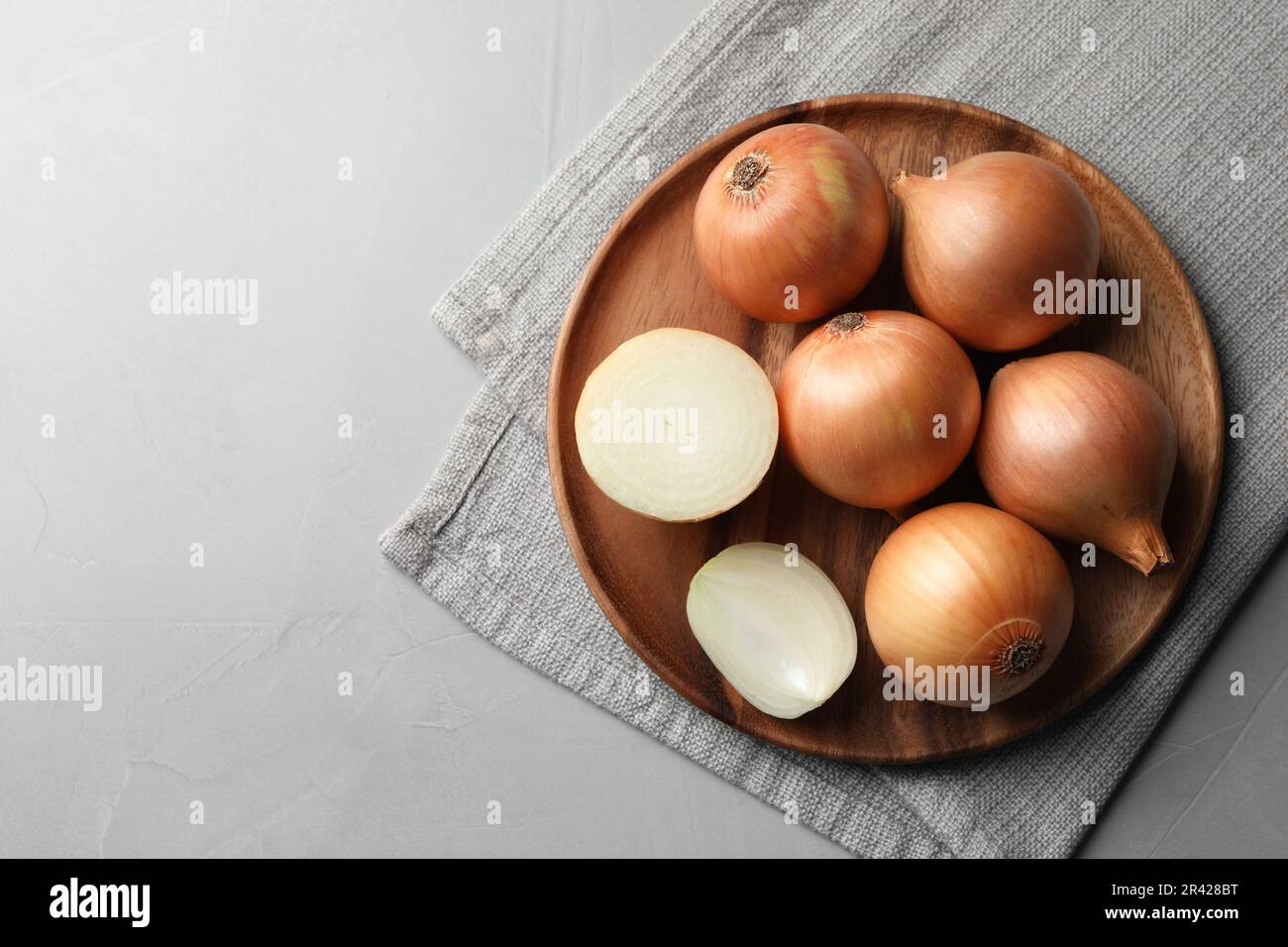 Whole and cut onions on light grey textured table, top view. Space for ...
