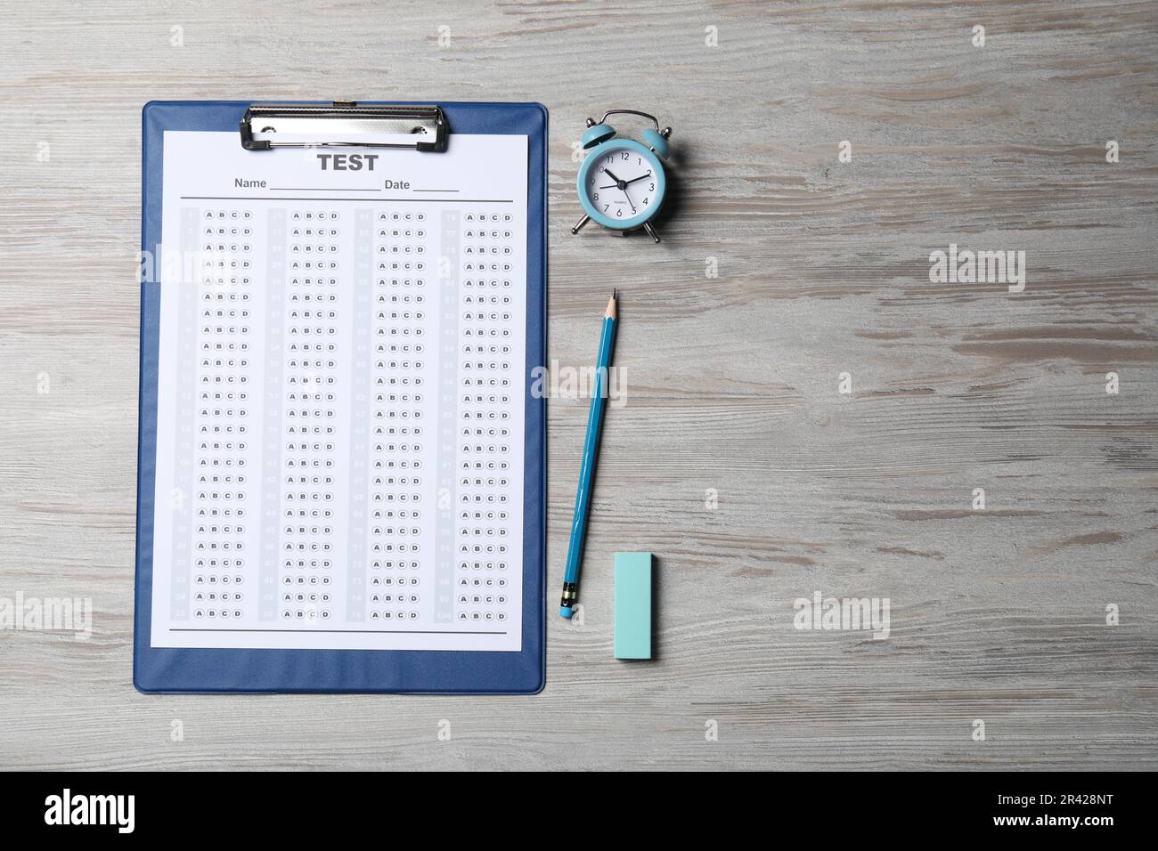 Clipboard with answer sheet, pencil and alarm clock on light wooden table, flat lay and space ...