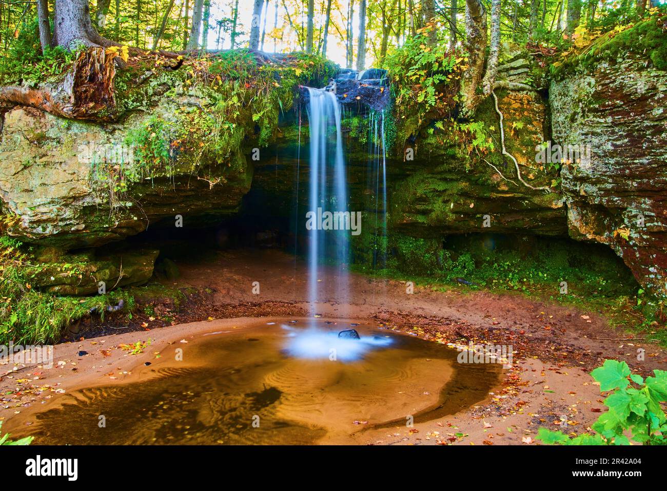 Tall blue waterfall pouring over lichen, moss covered cliff edge into ...