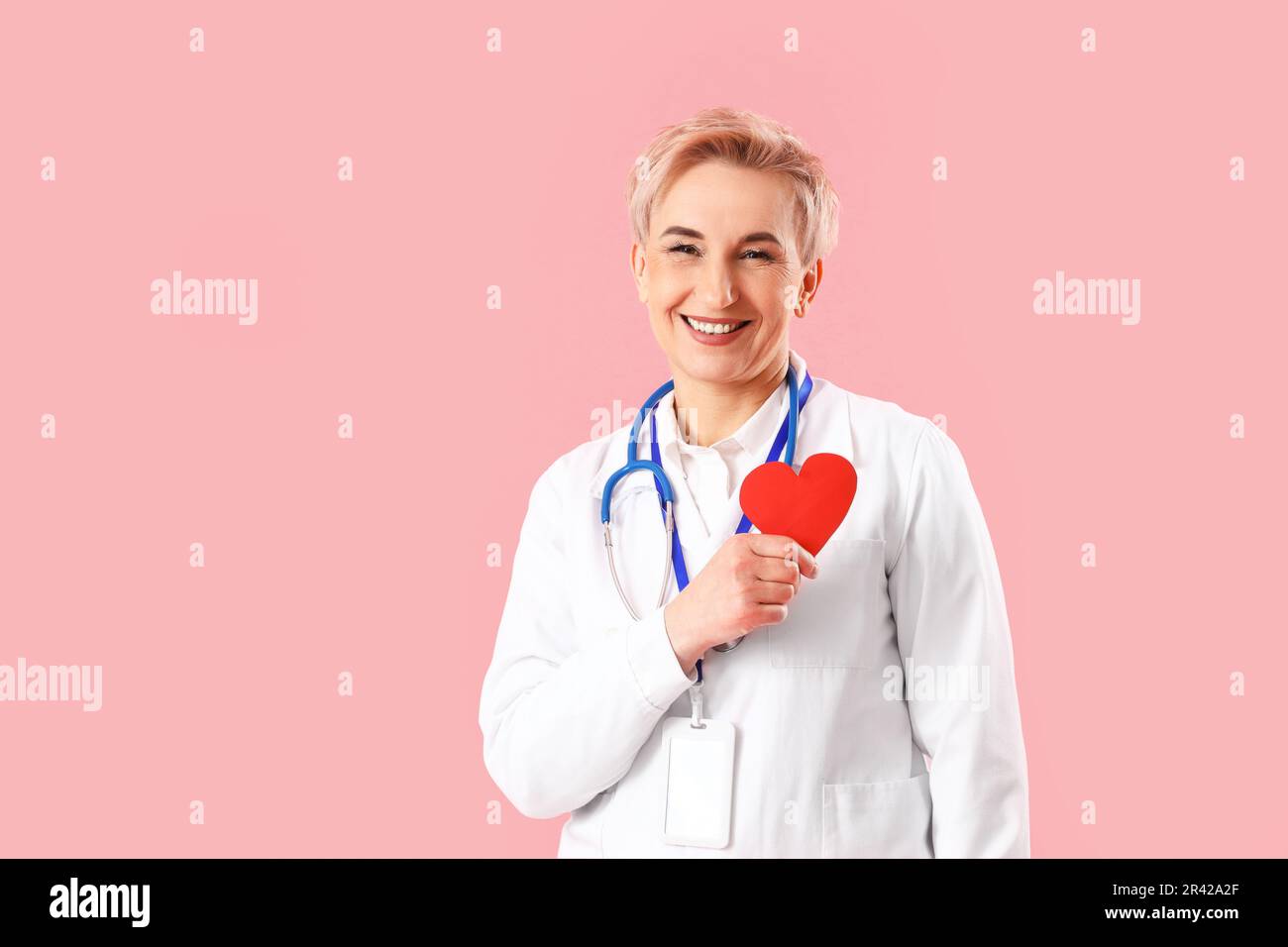 Mature female cardiologist with red heart on pink background Stock ...
