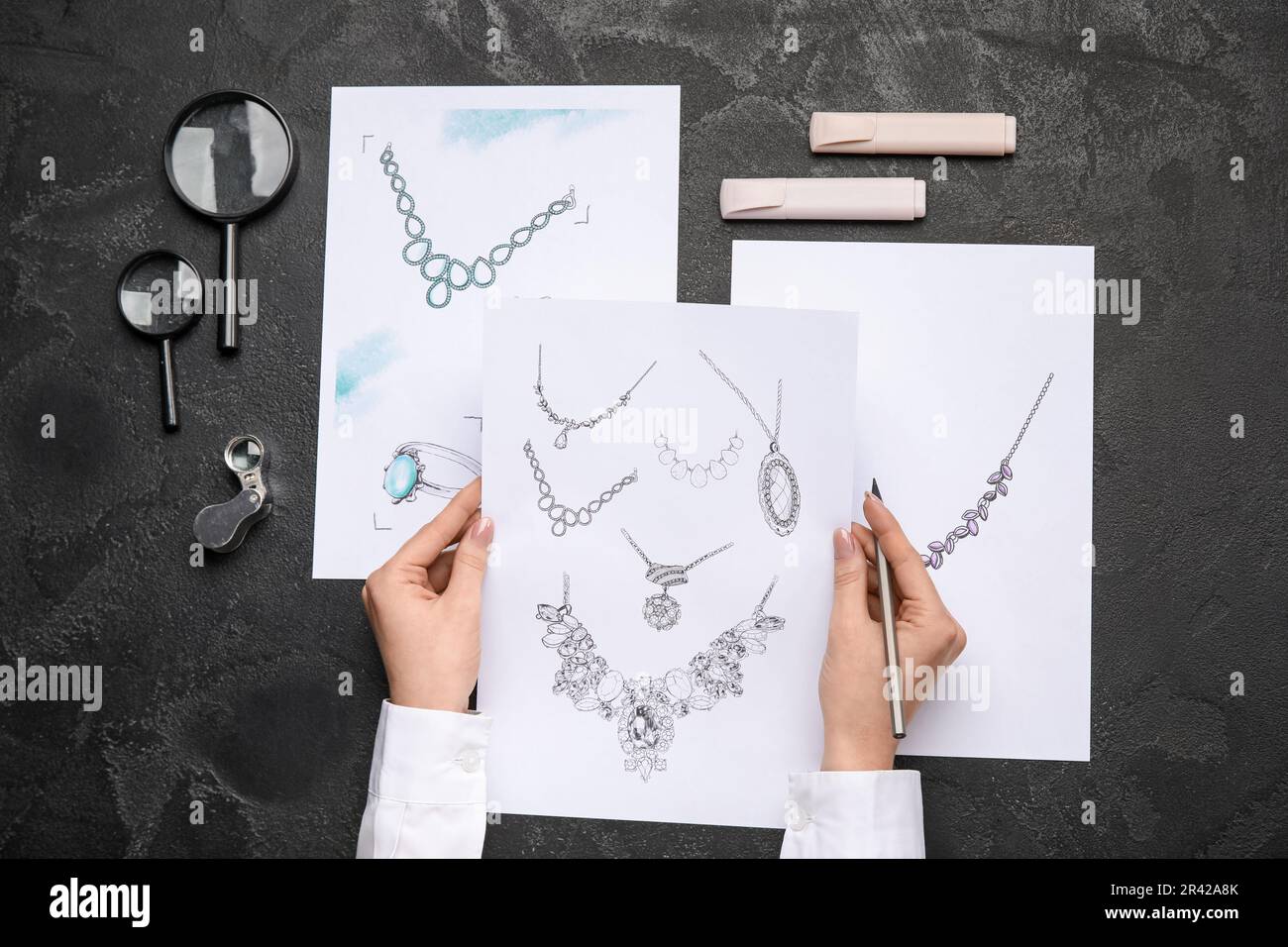 Female jeweler with drawings of adornment on dark table, top view Stock ...