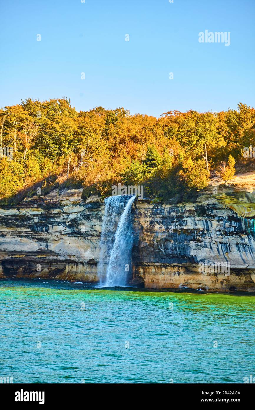 Summer forest behind tall waterfall flowing into lake or ocean with ...