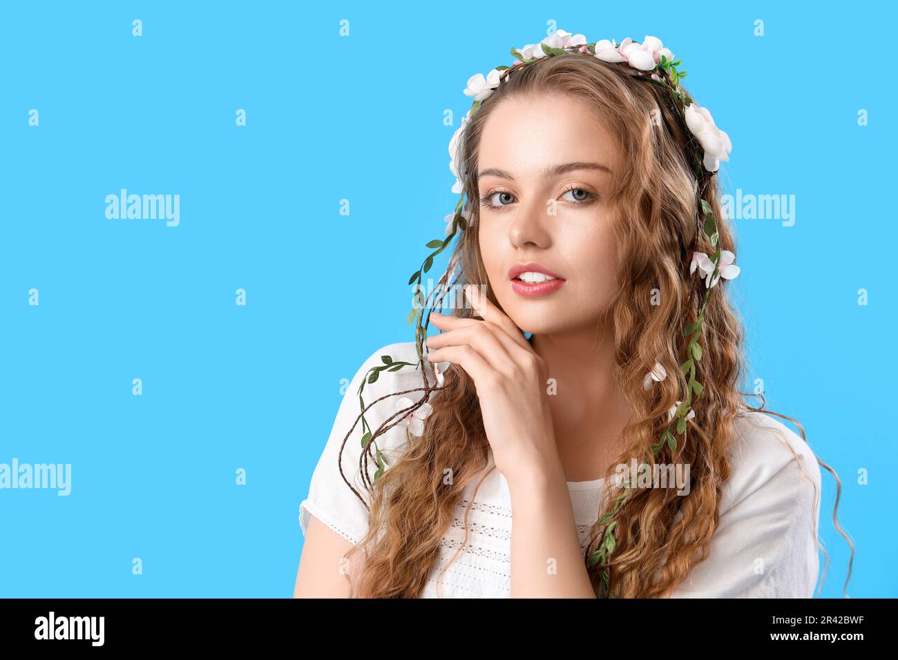 Beautiful young woman with flowers in her hair on blue background ...