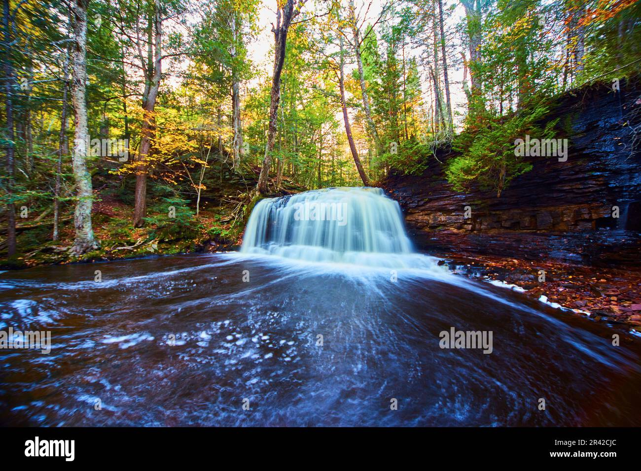 Fast flowing water from large waterfall with black and brown cliff and ...