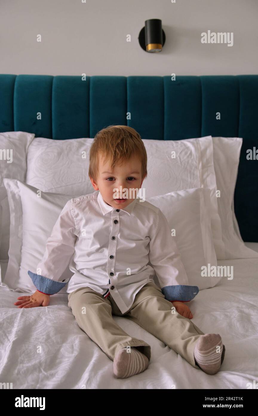 Little boy dressed for celebration sitting on a bed Stock Photo - Alamy