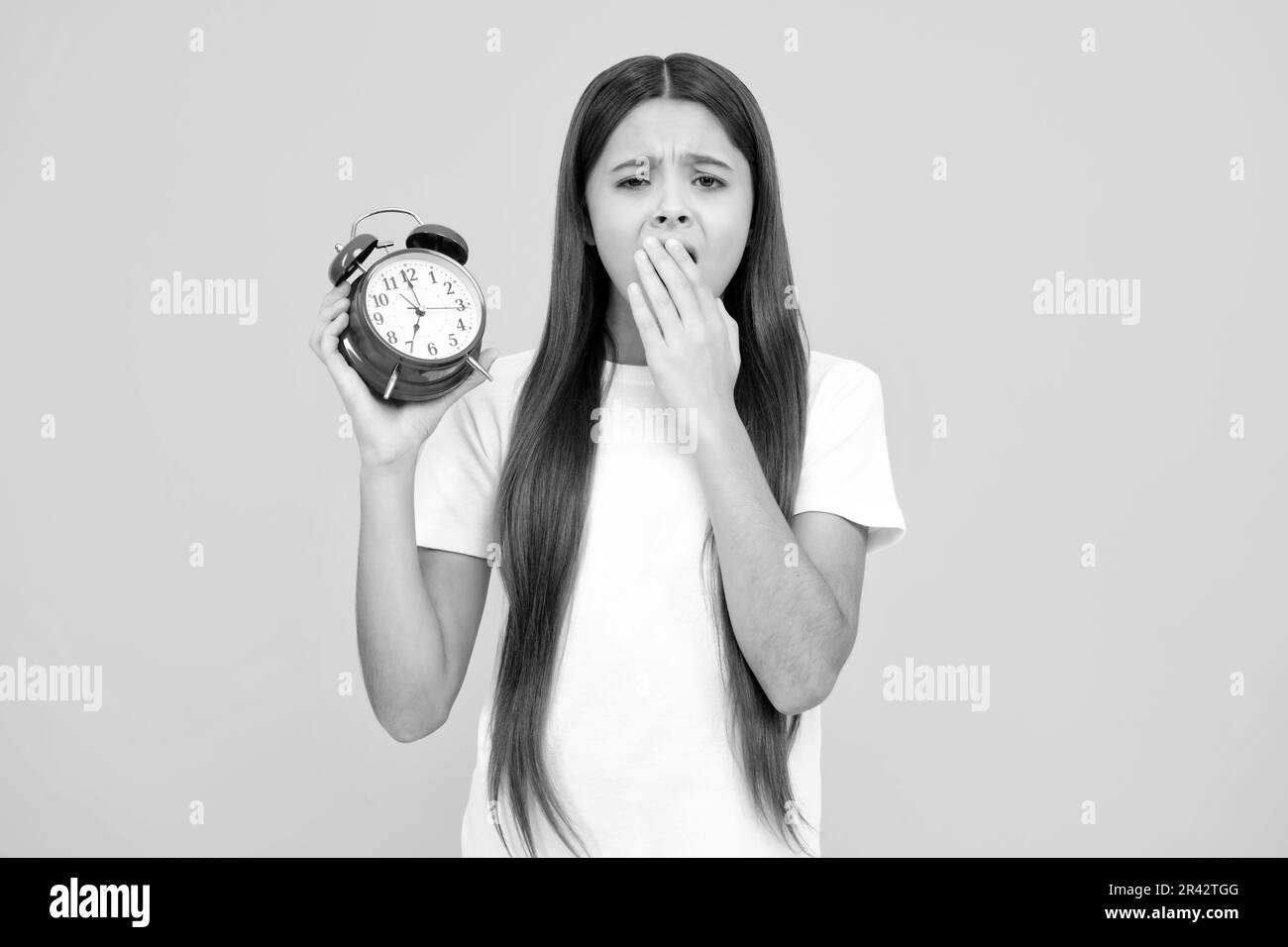 Tired and bored teenager girl. Child holding clock over yellow ...