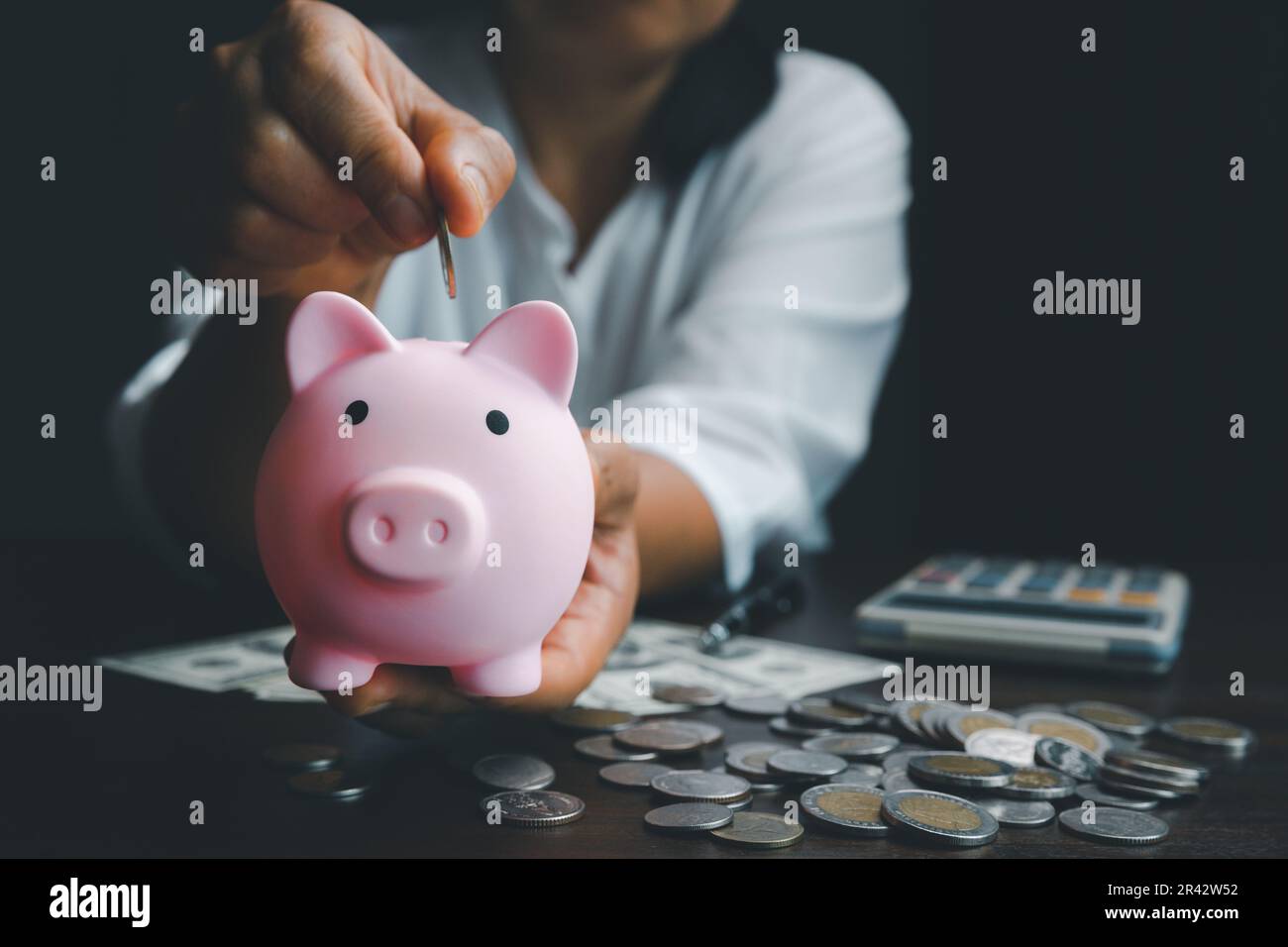 Business asian woman hand put coins in piggy bank on wood table ...