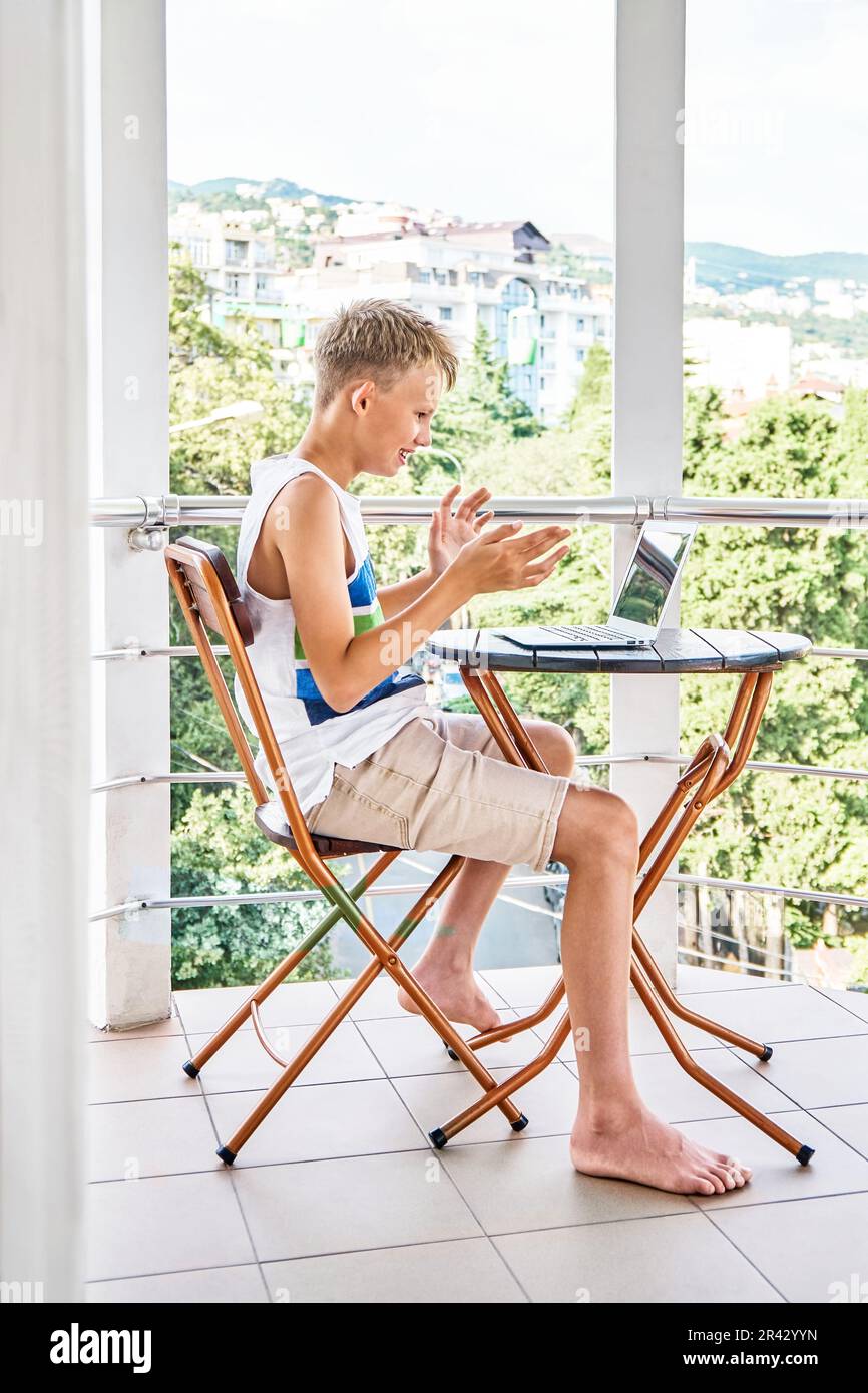 Boy sitting on balcony with happy expression communicates on a video ...