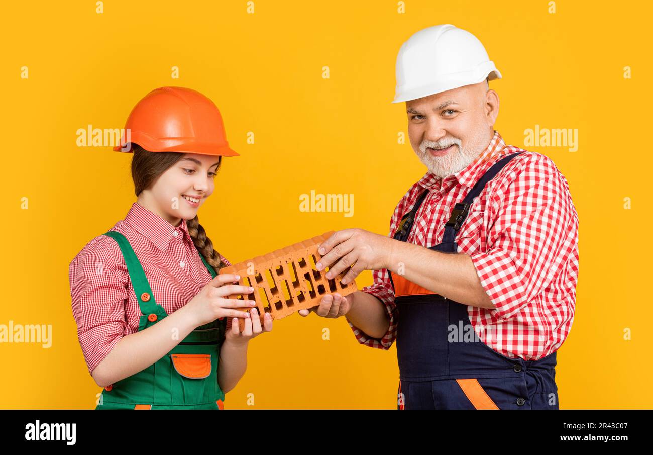 happy girl and grandfather bricklayer in helmet on yellow background ...