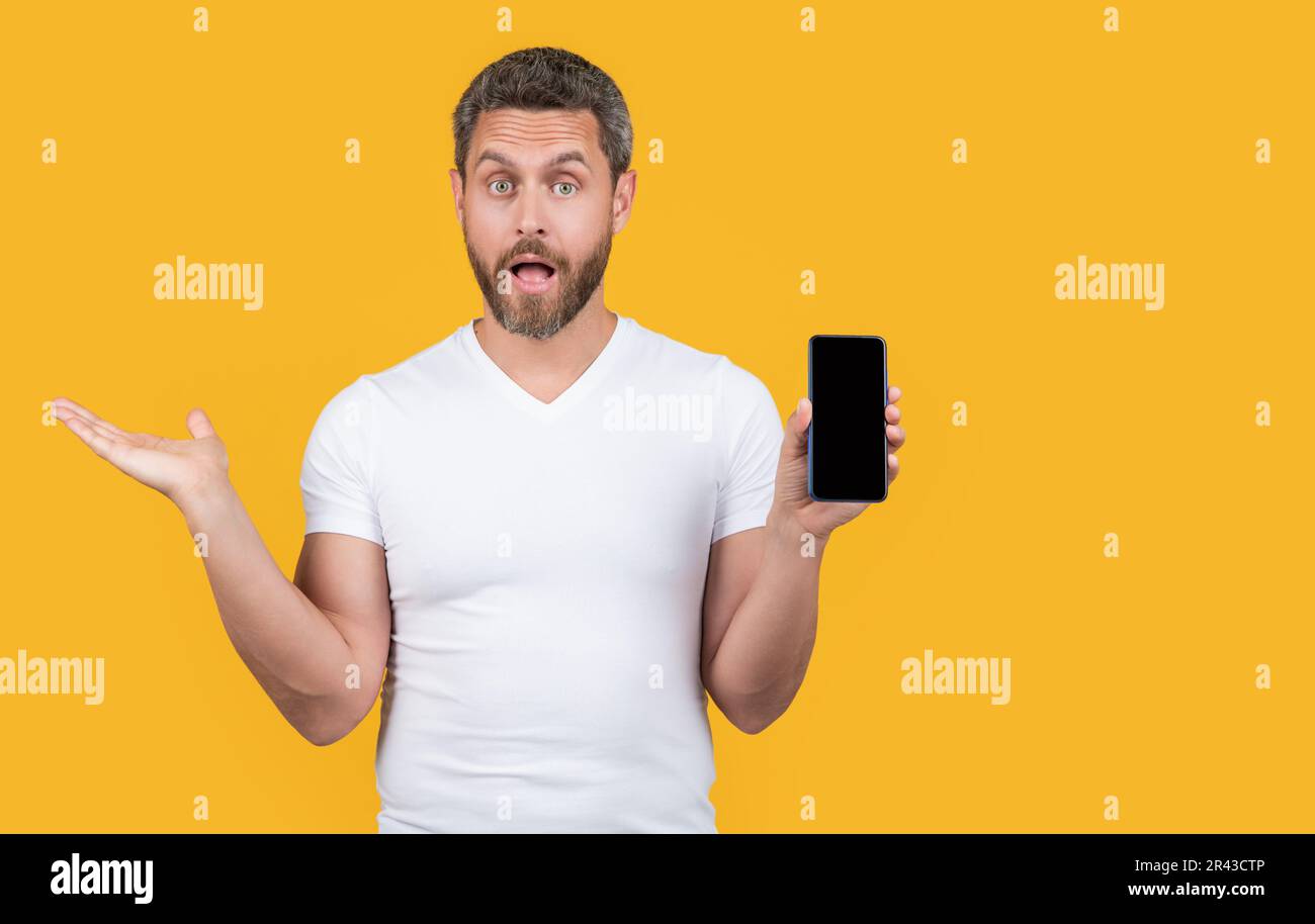 surprised man showing phone screen isolated on yellow background. man ...