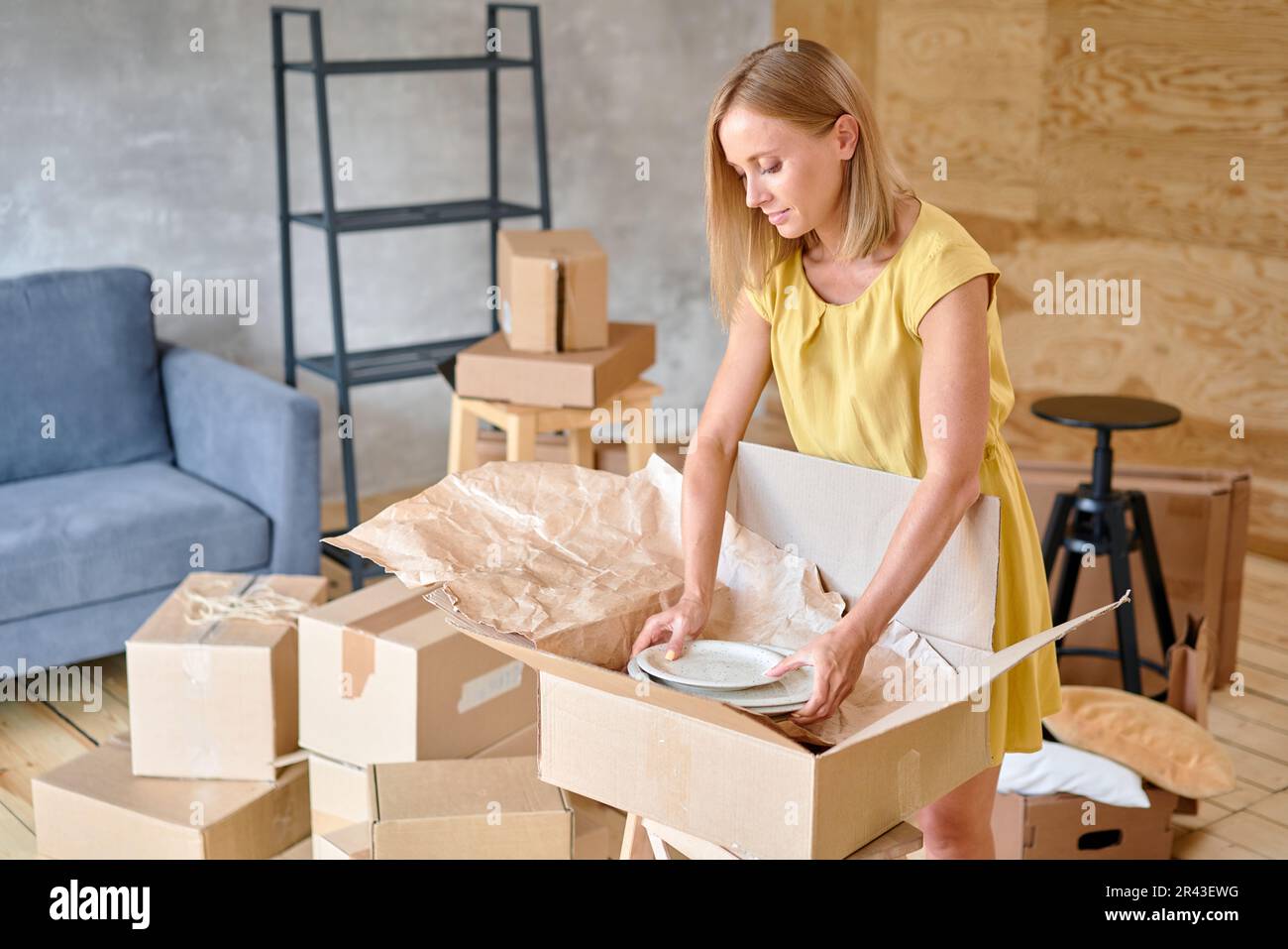 Young girl packing plates into the boxes ready to move. Woman unpacking ...
