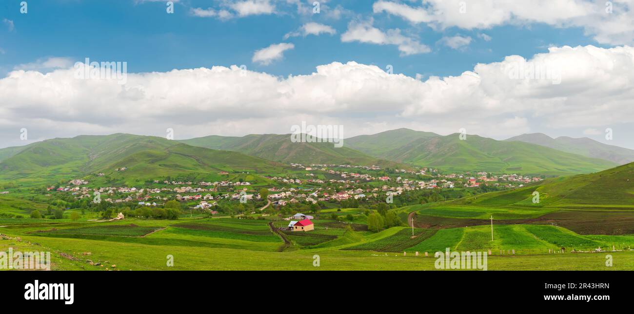 Wide panoramic view of a village at the foot of green mountains in ...