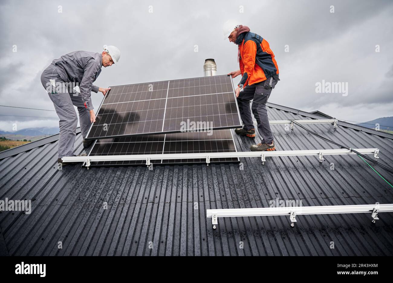 Technicians installing solar panel system on roof of house. Men Installers in helmets carrying ...