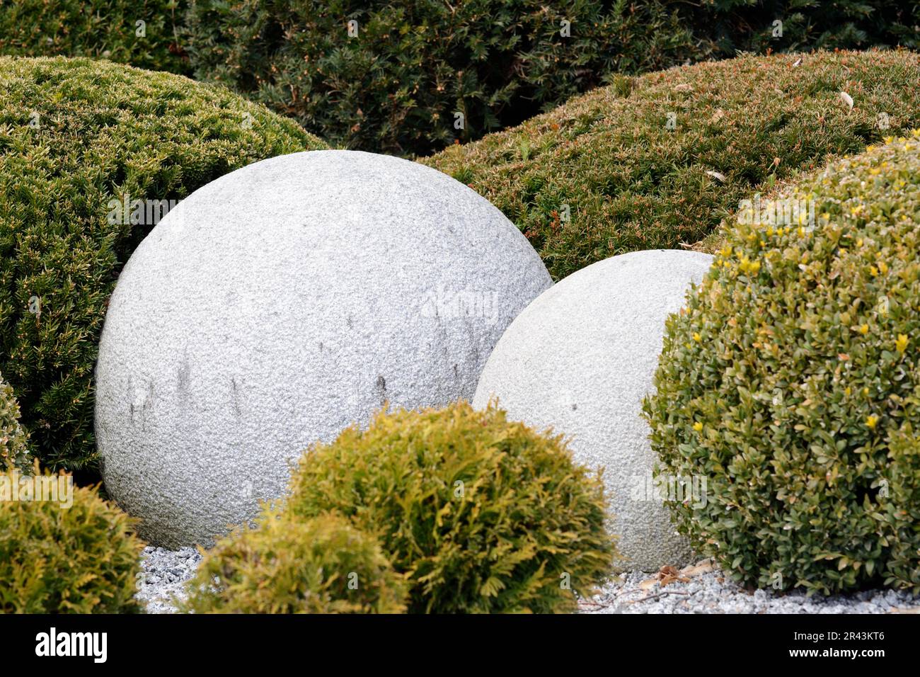 Granite stone balls and bushes in a park Stock Photo - Alamy