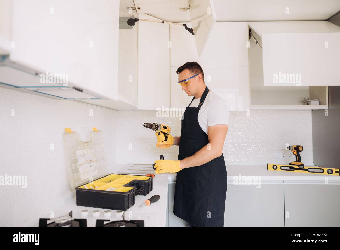 Maintenance man installing kitchen furniture in a black apron and ...