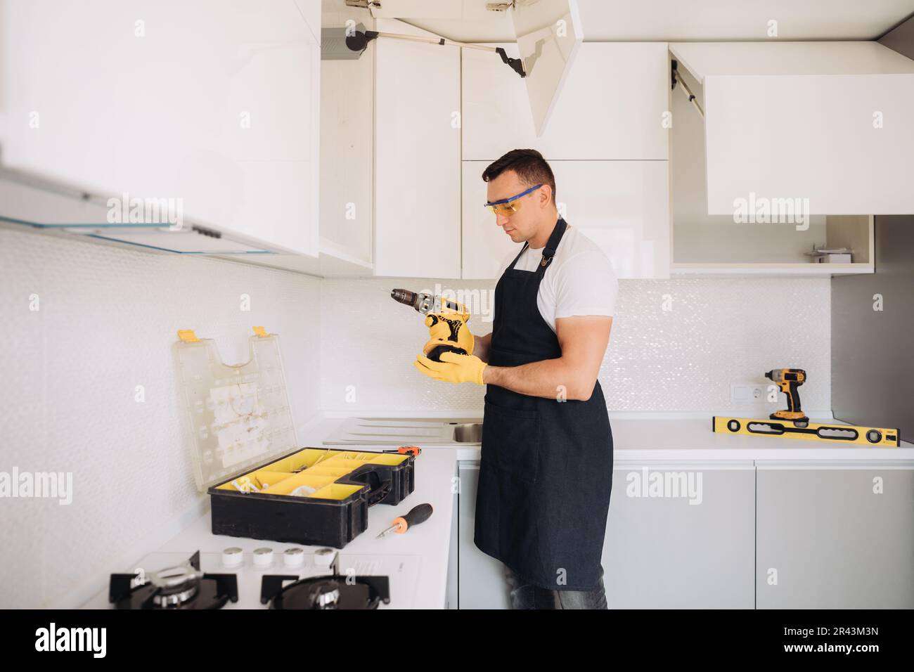 Maintenance man installing kitchen furniture in a black apron and ...